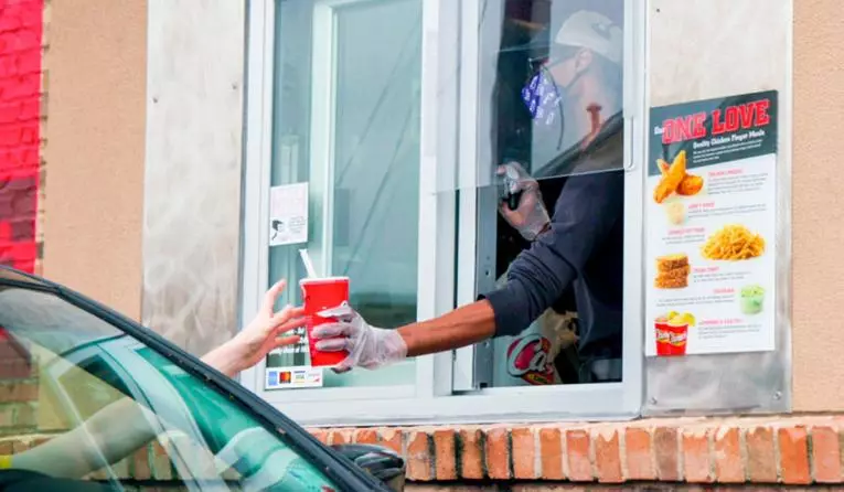 La veturoficisto de Raising Cane donas manĝaĵon tra la fenestro.