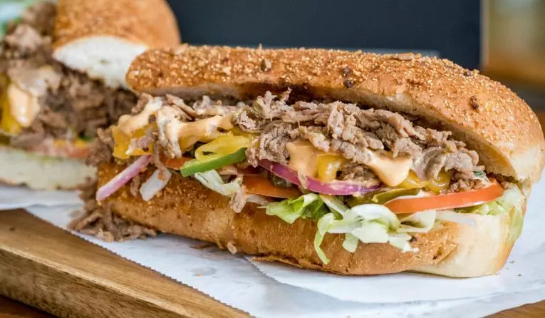 Subway's Chipotle Cheesesteak gemaakt met steak, geraspte Monterey cheddar kaas, knapperige sla, gesneden tomaten, groene pepers, rode ui en jalapeños en aangekleed met een rokerige Chipotle Southwest saus.