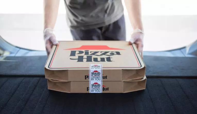 Ein Mitarbeiter von Pizza Hut packt zwei Kartons in ein Auto.