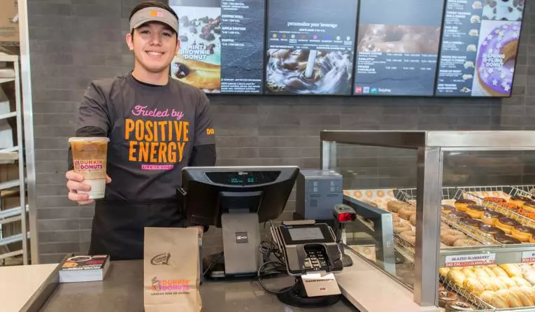 Dunkin' çalışanı bir fincan kahve uzatıyor.