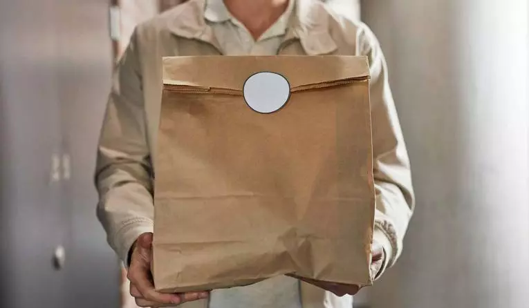 Un empregado dun restaurante levando unha bolsa de papel marrón con comida.