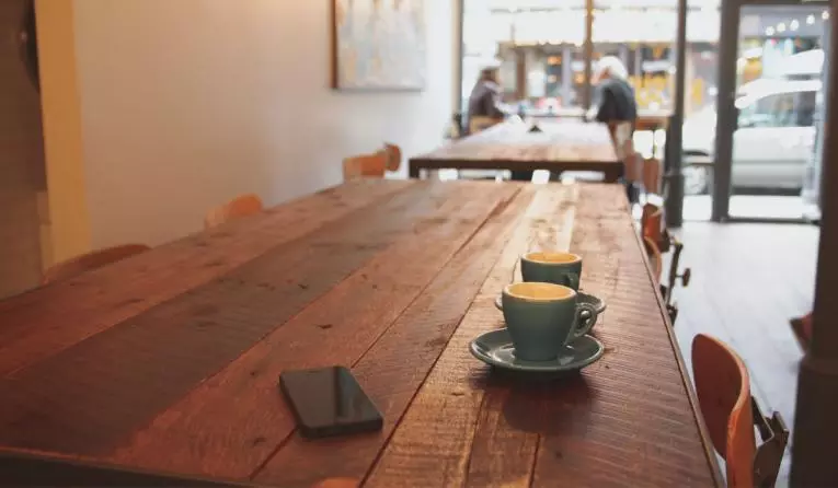 Meja kayu dengan dua cawan kopi di atasnya.