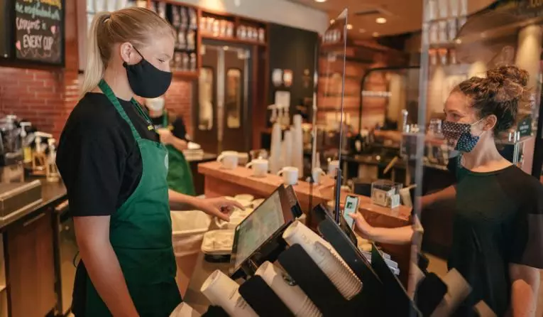 Starbucks-ის თანამშრომელი ნიღბით ემსახურება მომხმარებელს.