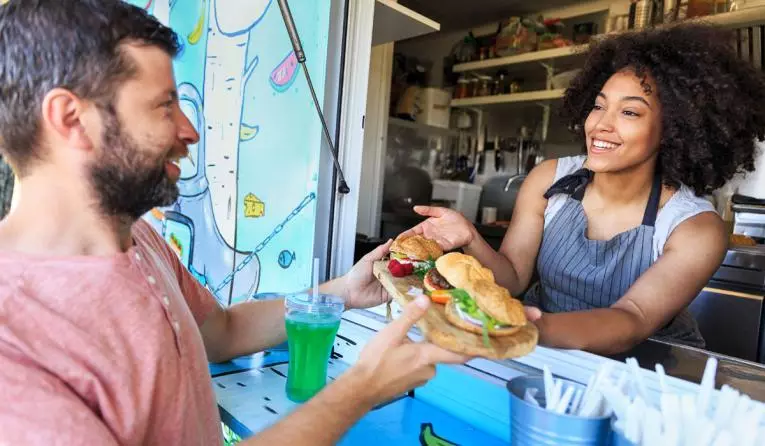 Žena podává zákazníkovi jídlo oknem food trucku.