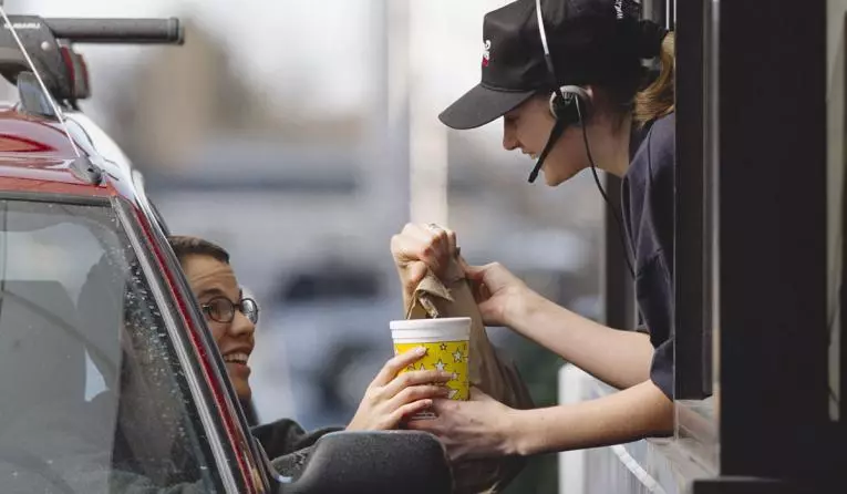 E Restaurant Employé iwwerhëlt engem Client Iessen duerch eng Drive-Thru Fënster.