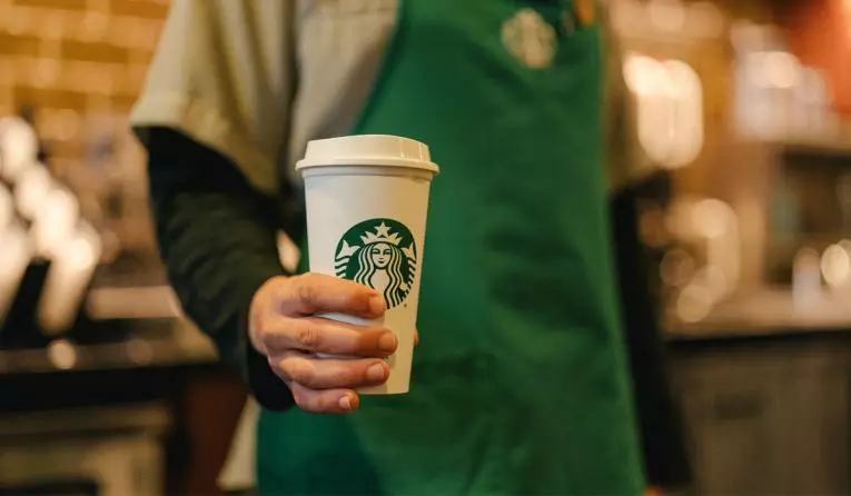 Gweithiwr Starbucks yn dal cwpan.