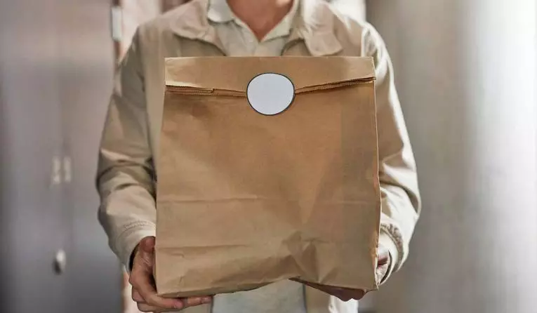 Isang empleyado ng restaurant na may dalang brown paper bag ng pagkain.