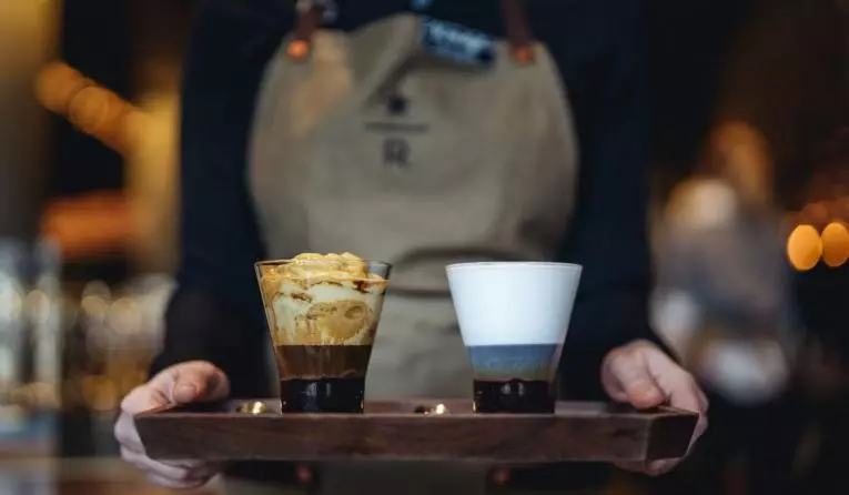 Starbucks Barista သည် ဗန်းတစ်ခုပေါ်တွင် ကော်ဖီနှစ်ခွက်ကို ကိုင်ထားသည်။