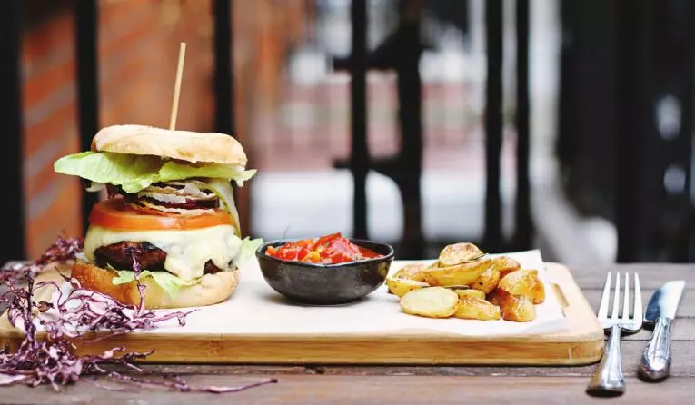 Hamburgers, kartupeļi un kečups uz koka šķīvja.