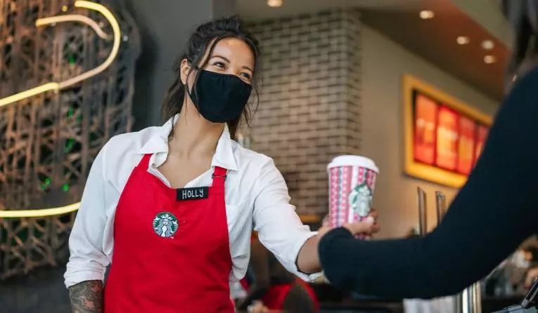 Pracownik Starbucksa podający klientowi drinka.